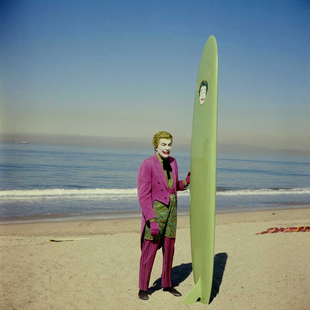 Cesar Romero as The Joker stands beside a green surfboard with a ...